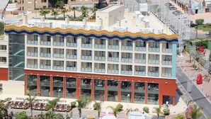Hotel de vários andares com marina comercial e placa indicando a praia, apresentando fachada moderna com grandes janelas e varandas.