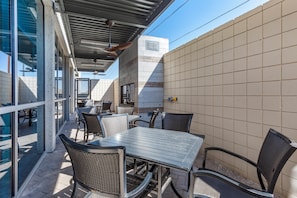 Uma área de terraço externa com mesas e cadeiras, um espaço de estar coberto e vista para a rua.