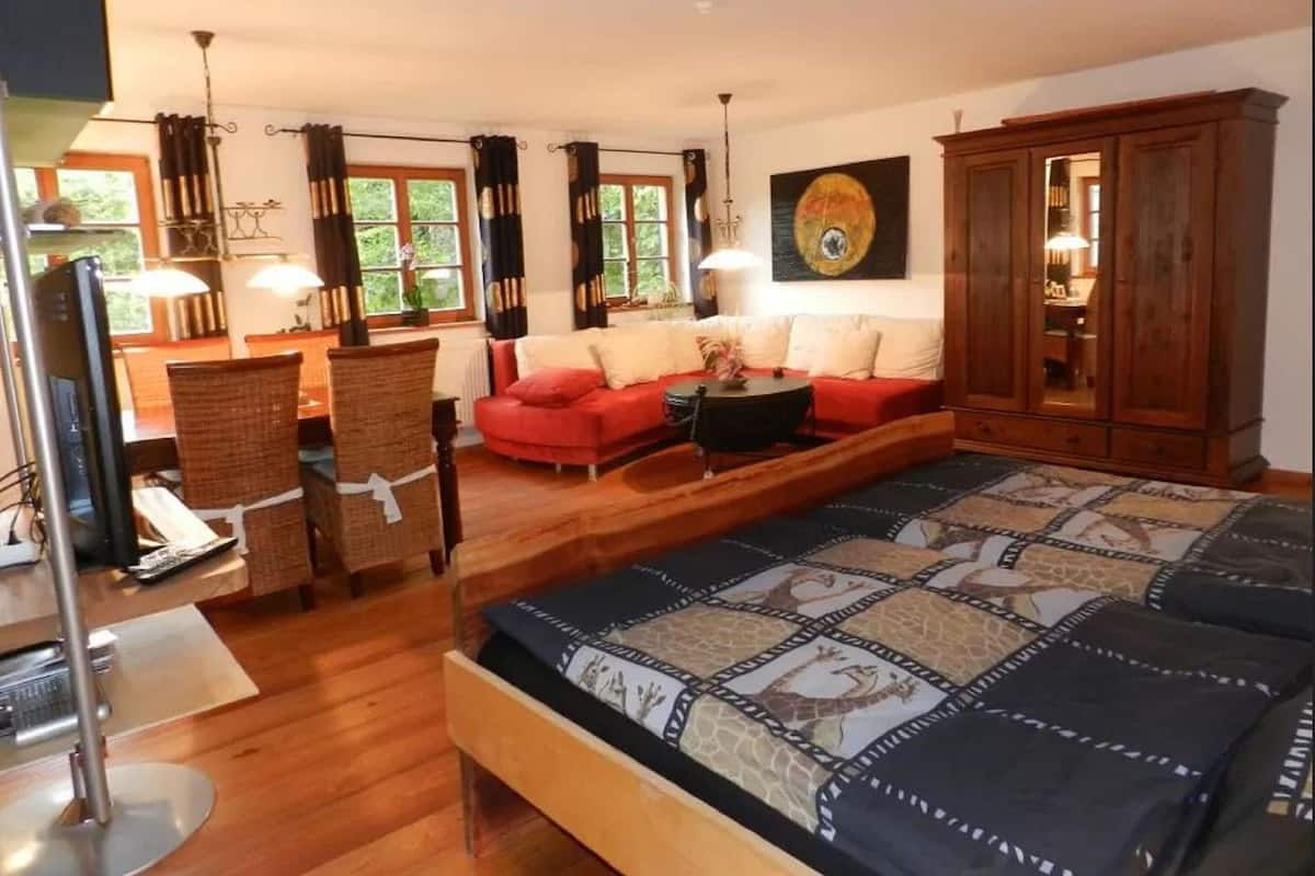 Um quarto aconchegante com uma cama grande, um sofá vermelho, um armário de madeira e um espaço de refeições com cadeiras de vime e uma mesa.