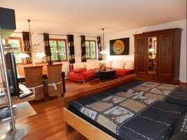 Um quarto aconchegante com uma cama grande, um sofá vermelho, um armário de madeira e um espaço de refeições com cadeiras de vime e uma mesa.