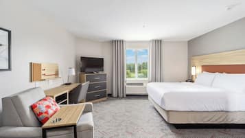 Quarto de hotel com cama, escrivaninha com cadeira, televisão e janela com cortinas.