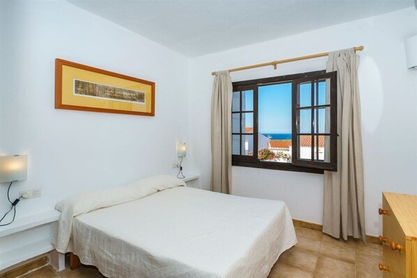 Quarto com cama, janela com cortinas, luminária na parede e um quadro emoldurado.