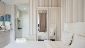 Quarto de hotel com cama, banheiro com cortina de chuveiro e uma área de cozinha compacta.