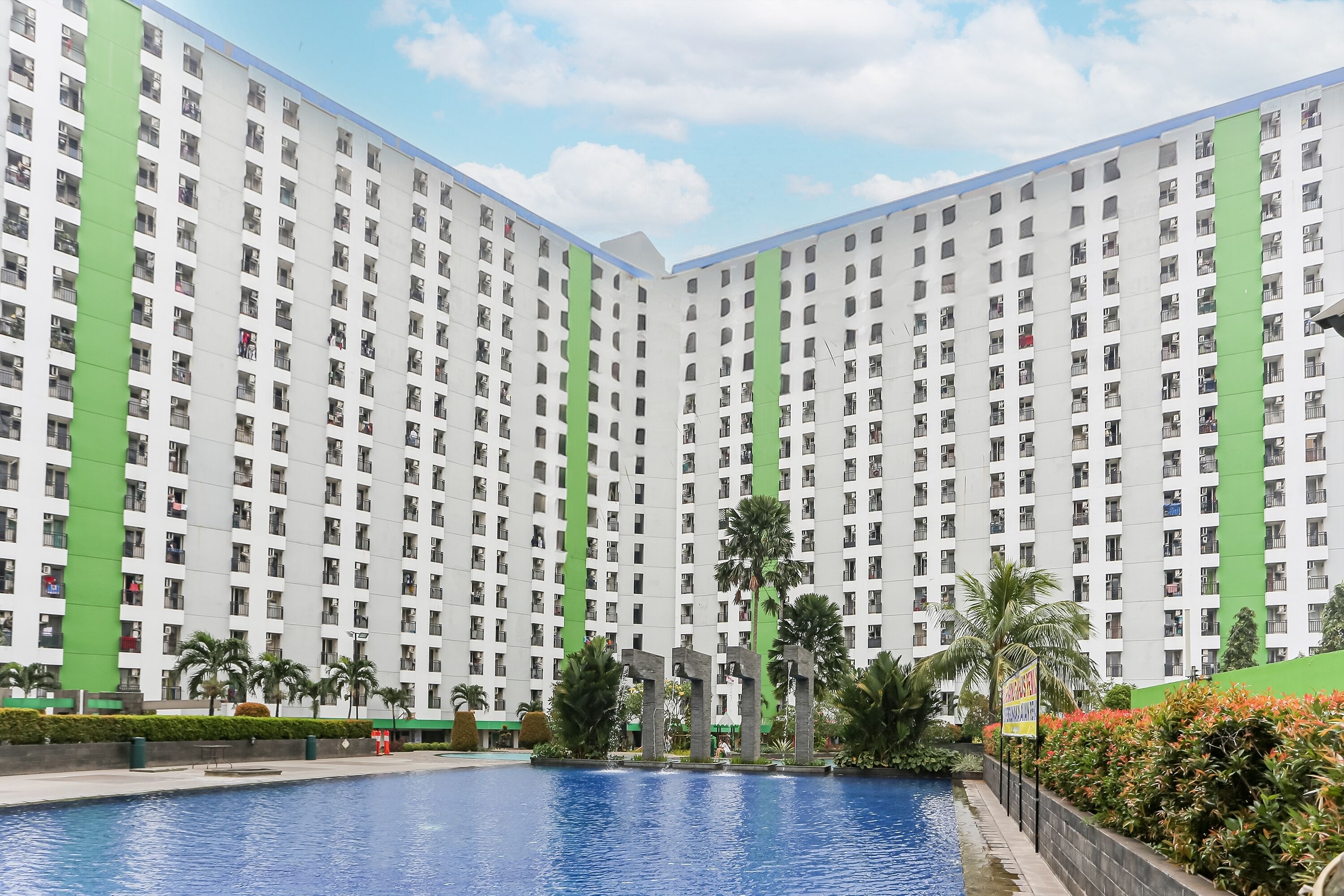 Um edifício residencial alto com várias varandas, piscina e palmeiras.