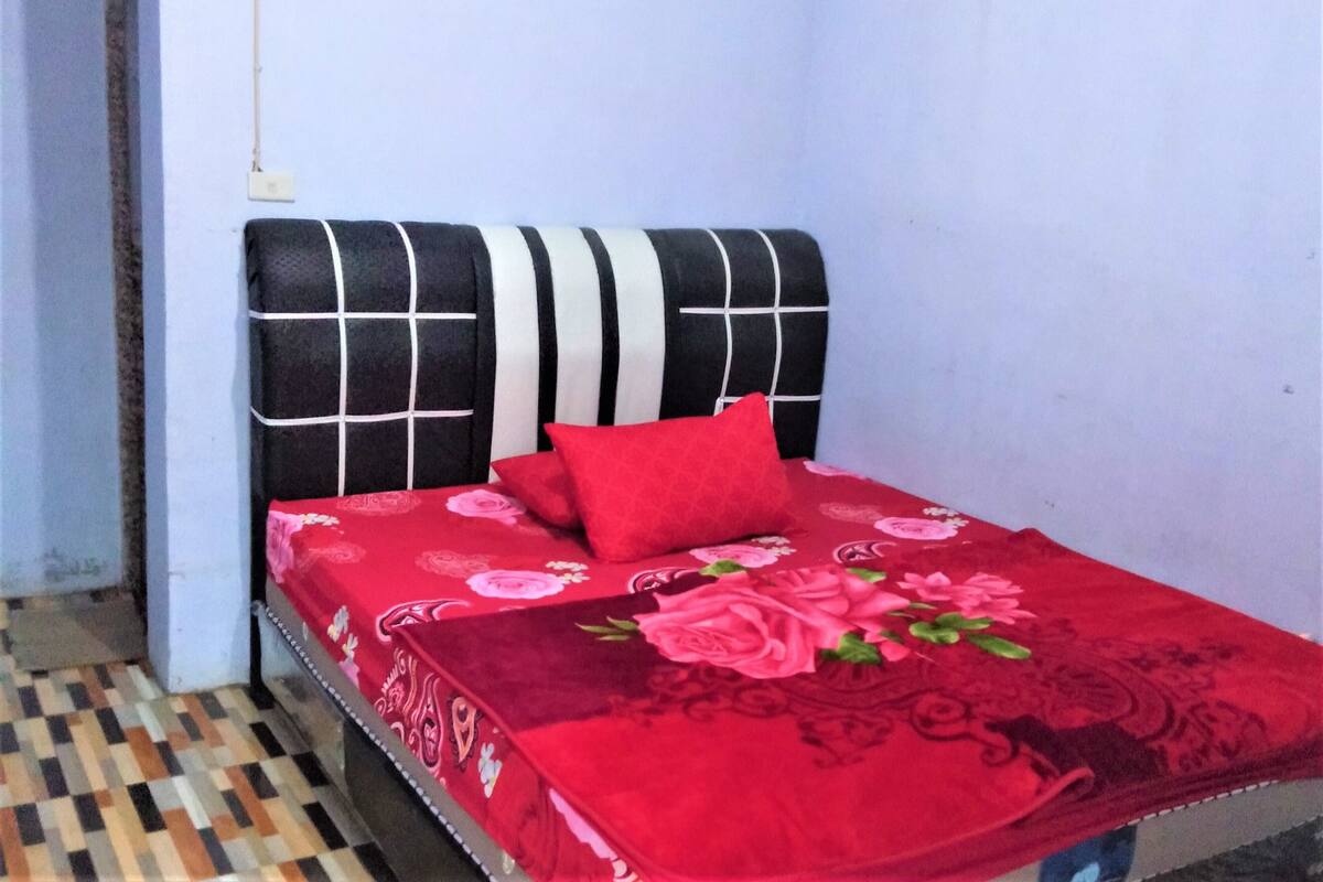 Uma cama de solteiro com cabeceira preta e branca, edredom floral vermelho e travesseiro vermelho.