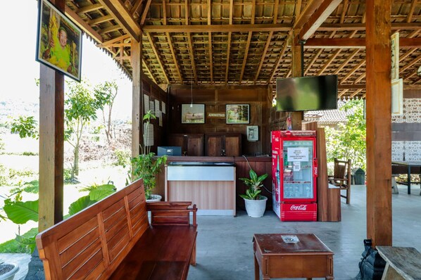 Interior em madeira com uma mesa de recepção, uma televisão e um refrigerador de Coca-Cola.