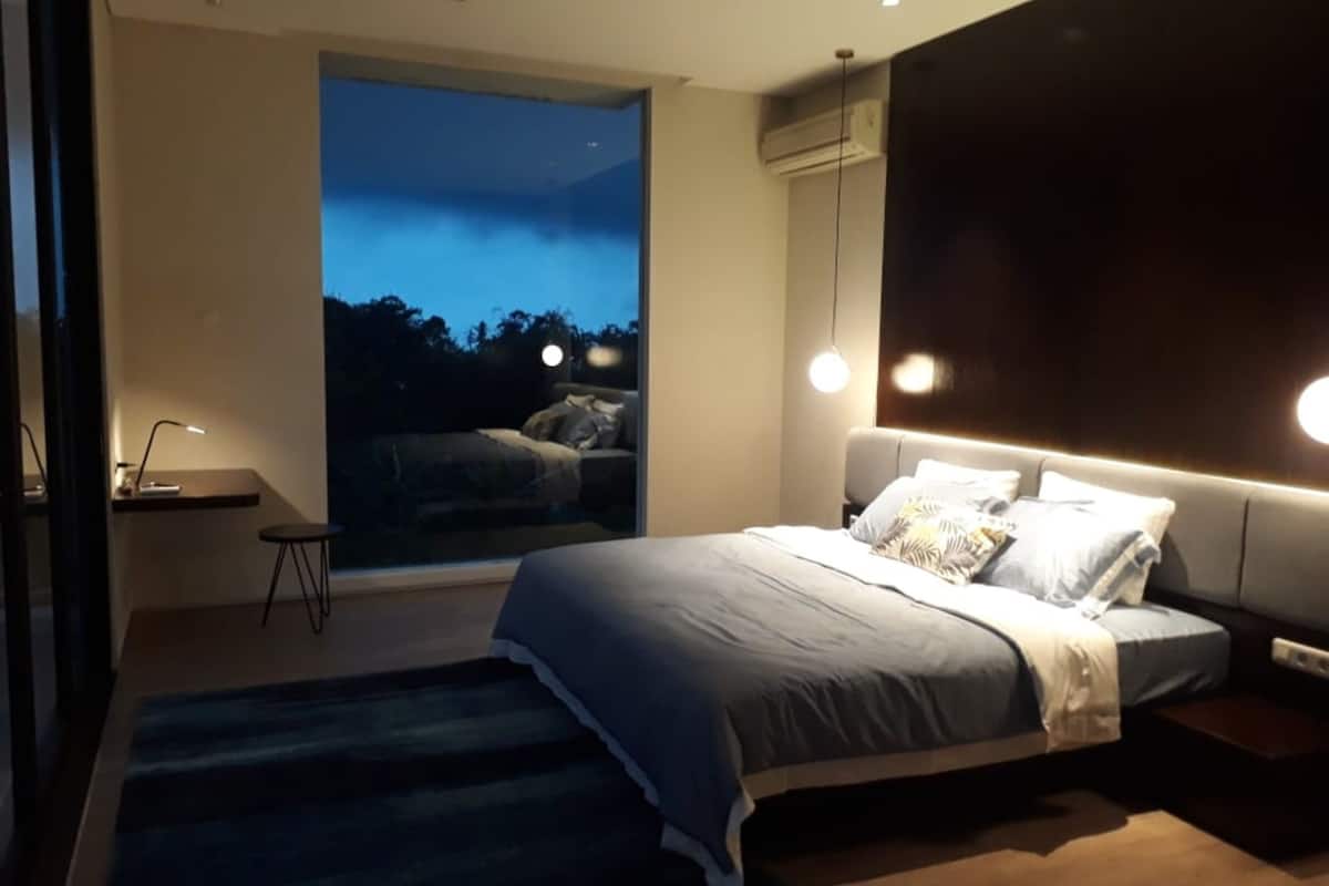 Quarto moderno com uma janela grande, cama com cabeceira e mesa de cabeceira.