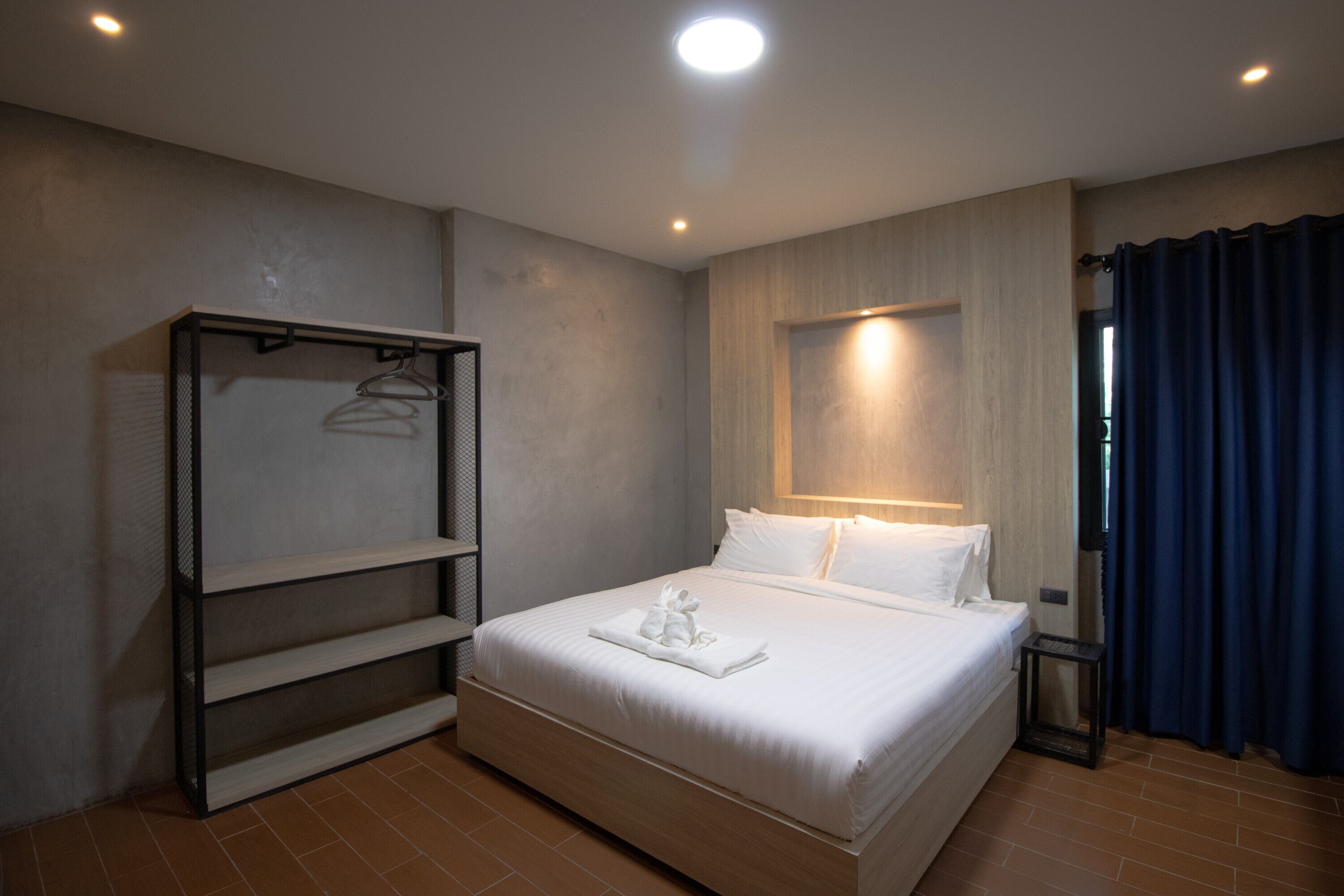 Quarto de hotel moderno com uma cama grande, um guarda-roupa com espaço para pendurar e uma pequena mesa de cabeceira.