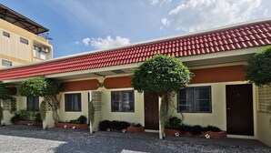 Um edifício com telhado de telhas vermelhas, várias janelas e entrada por um caminho de cascalho.