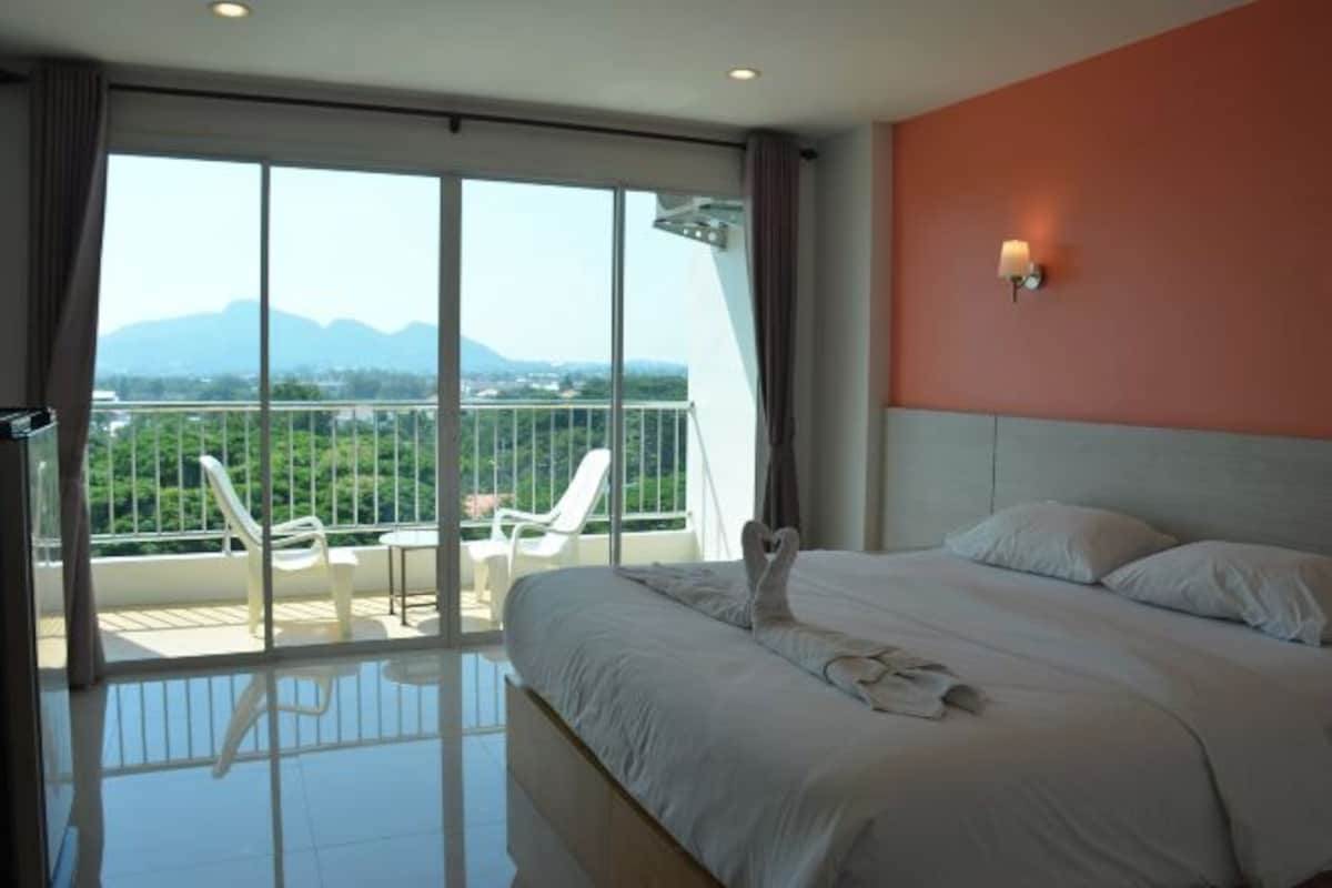 Quarto de hotel com uma cama grande, varanda com cadeiras e vista para montanhas.