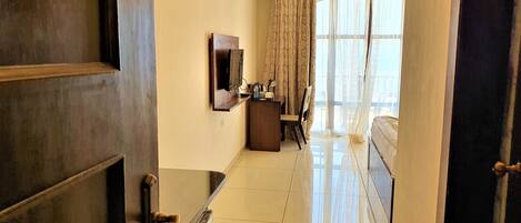 Quarto de hotel com cama, escrivaninha com cadeira, televisão e janela com cortinas.