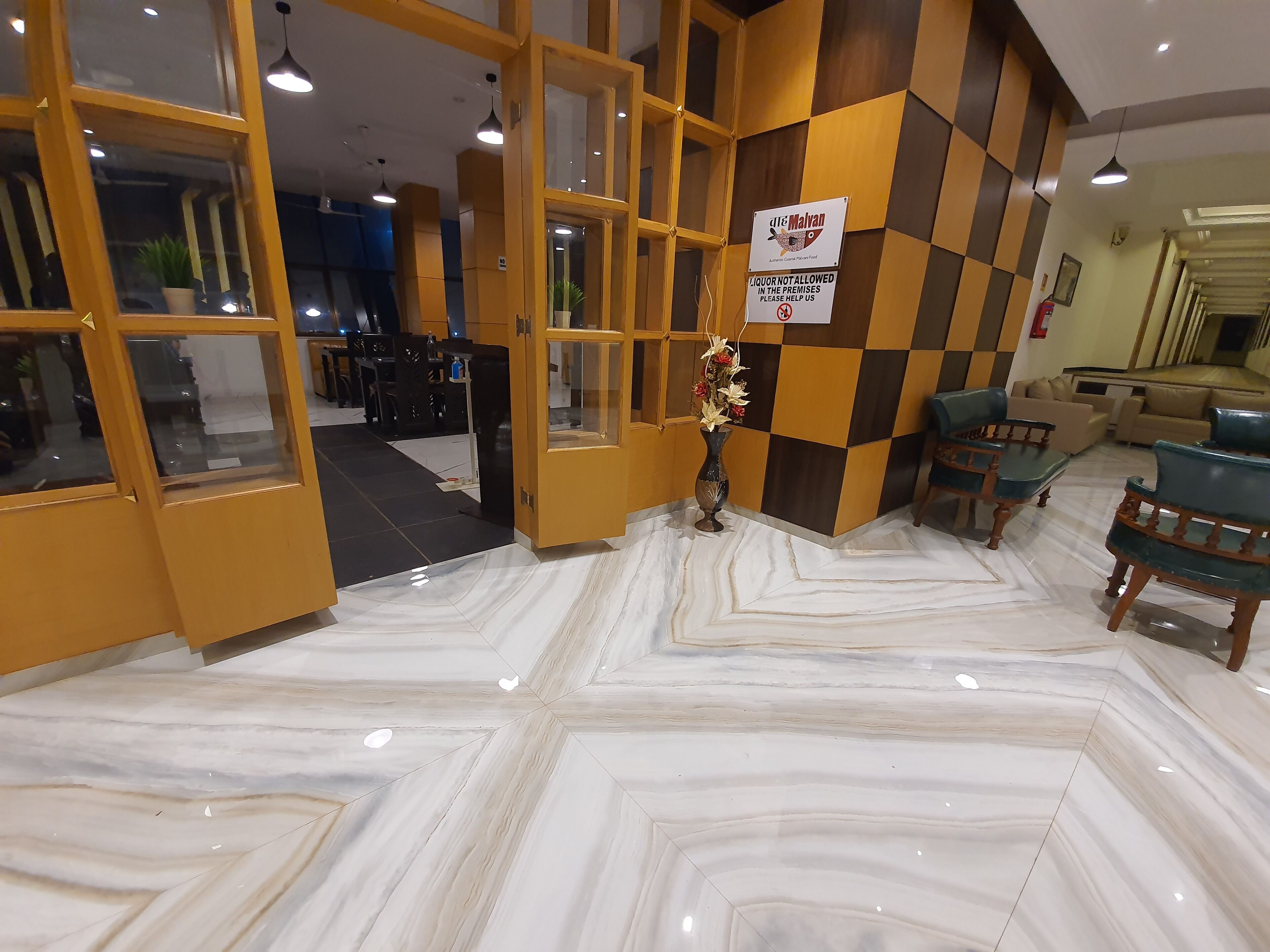 Um saguão de hotel com padrão quadriculado na parede, uma placa proibindo bebidas alcoólicas e uma área de recepção com assentos.