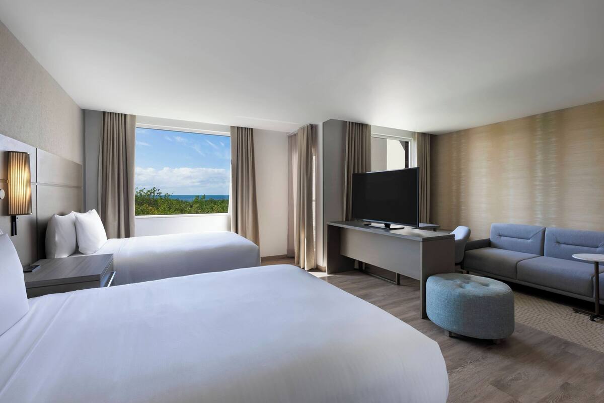 Quarto de hotel com duas camas, uma televisão, um sofá e uma escrivaninha.