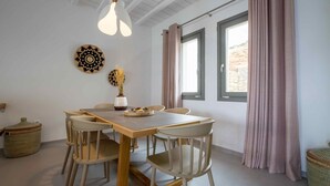 Uma sala de jantar com uma mesa de madeira, quatro cadeiras, um vaso com flores e um prato decorativo pendurado na parede.