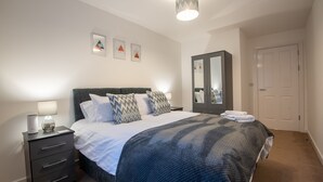 Um quarto bem organizado com cama, mesa de cabeceira, abajur e guarda-roupa.
