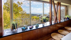 Cozinha moderna com grandes janelas, armários de madeira e vista para árvores e paisagem distante.