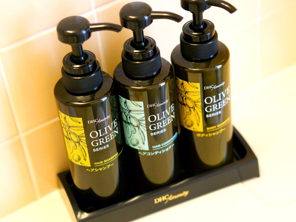 Três frascos de shampoo para cabelo verde-oliva num dispensador preto.