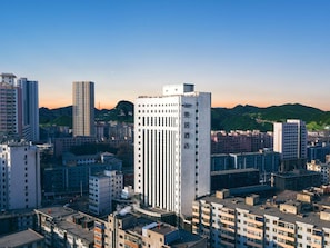 Um hotel moderno e alto, com vários andares, rodeado por outros edifícios e uma paisagem montanhosa ao fundo.