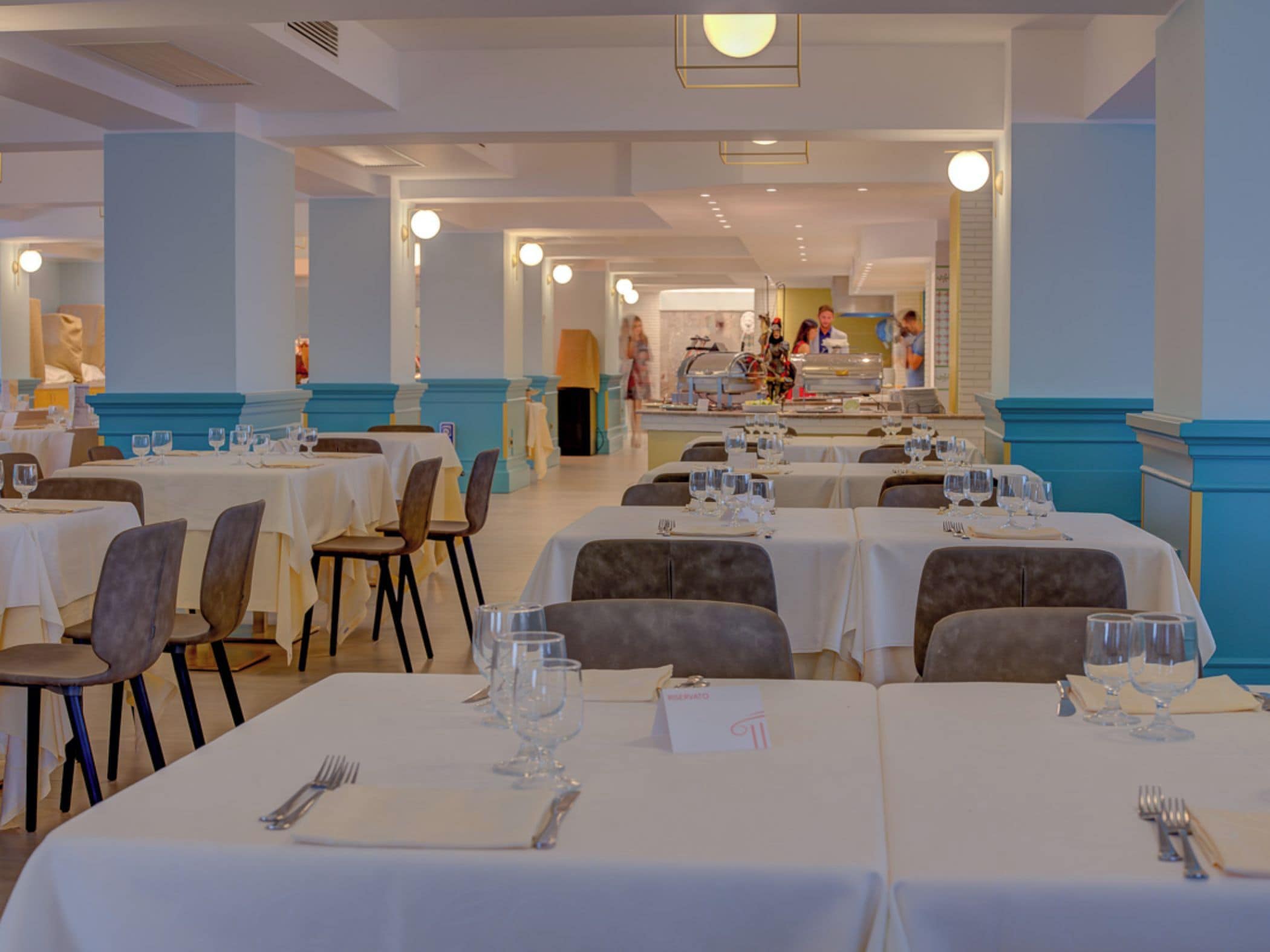 Restaurante com várias mesas, cada uma posta com talheres e copos, e uma paleta de cores azul e branca.