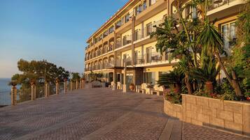 Um hotel com vários andares, varandas, um caminho pavimentado e vista para o mar.
