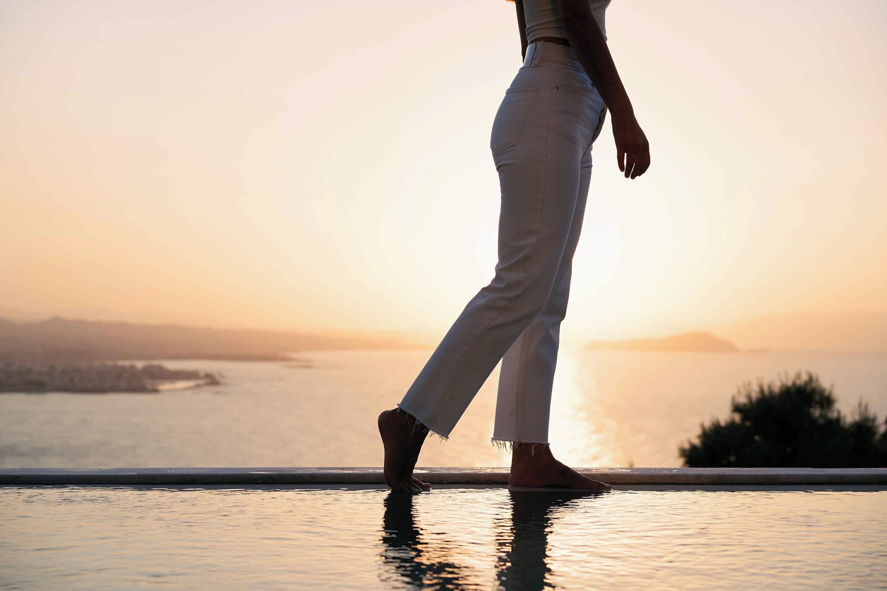 Uma pessoa está perto da piscina, com vista para o pôr do sol.