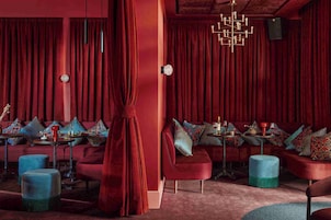 Quarto em tons de vermelho com um sofá, pufes e um candelabro.