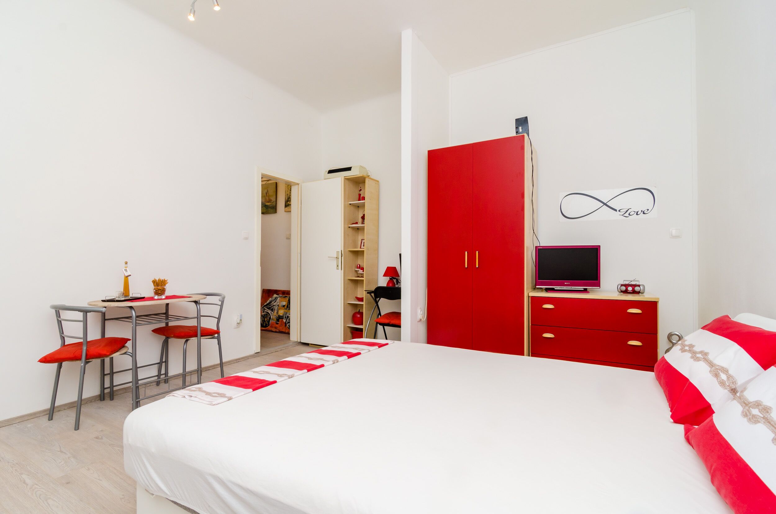 Quarto com uma cama, escrivaninha, cadeiras, guarda-roupa e televisão.
