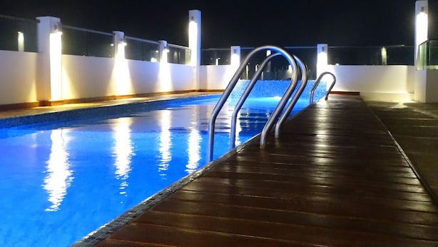 Piscina com grades de metal e deck de madeira à noite.