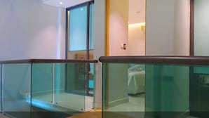 Quarto de hotel moderno com divisória de vidro, uma cama e um pequeno espaço de estar.