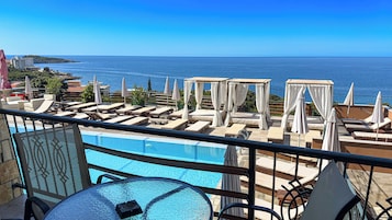 Área da piscina com espreguiçadeiras e guarda-sóis, com vista para um mar azul e límpido.