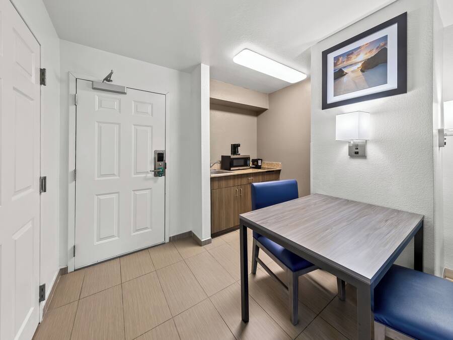 Quarto de hotel com mesa de jantar, cadeiras, micro-ondas e cafeteira.
