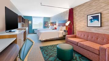 Quarto de hotel com cama, sofá, escrivaninha com cadeira, televisão e janela.