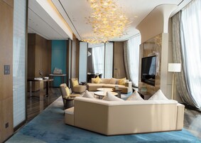 Quarto de hotel moderno com um sofá grande, poltronas, uma mesa de centro e uma televisão.