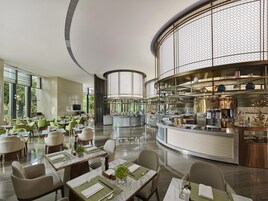 Um restaurante moderno com um bar central, mesas de jantar com jogos americanos verdes e um piano ao fundo.