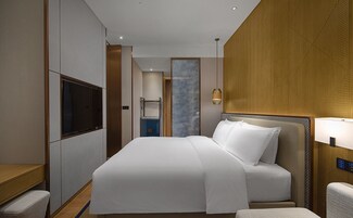 Quarto de hotel moderno com uma cama grande, televisão, escrivaninha e banheiro ao fundo.