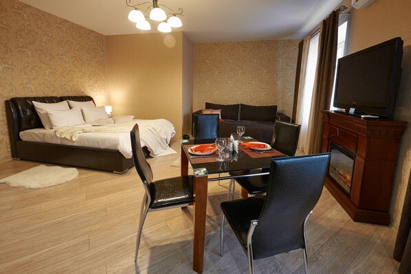 Quarto de hotel com cama, mesa de jantar com cadeiras, televisão e lareira.