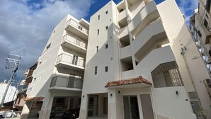 Um edifício residencial com vários andares, varandas, telhado de telhas e entrada com portão.