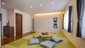 Quarto com tatames, mesa baixa com almofadas, cabideiro e uma obra de arte na parede.