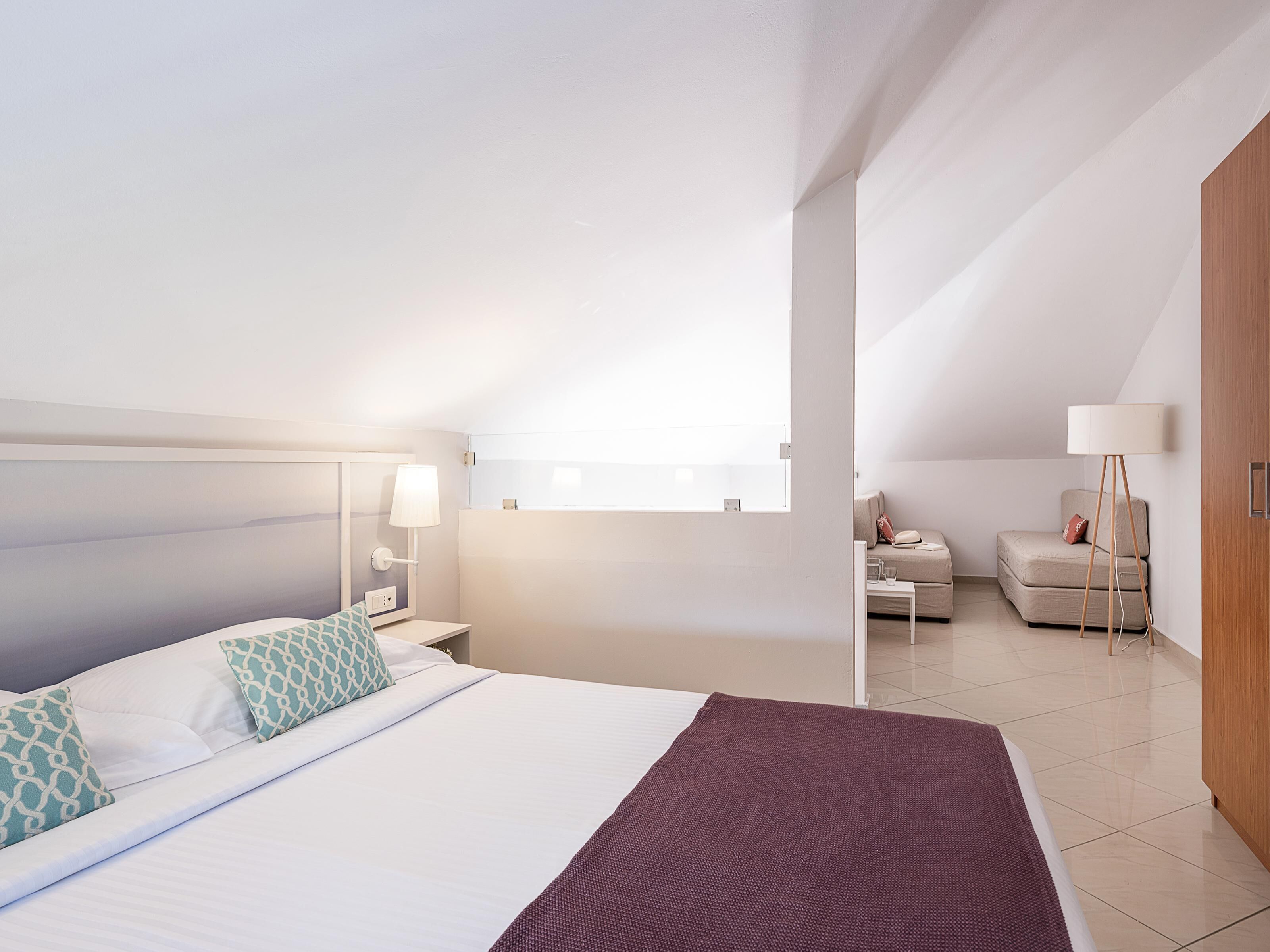 Quarto moderno com cama grande, mesa de cabeceira, luminária de chão, sofá e guarda-roupa.