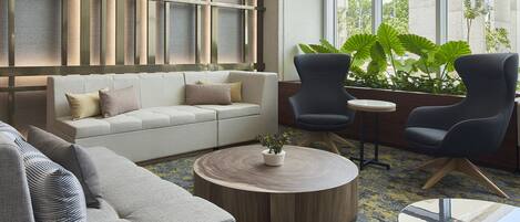 Uma sala de estar moderna com sofá, poltronas, mesa de centro e uma grande janela com vista para o verde.