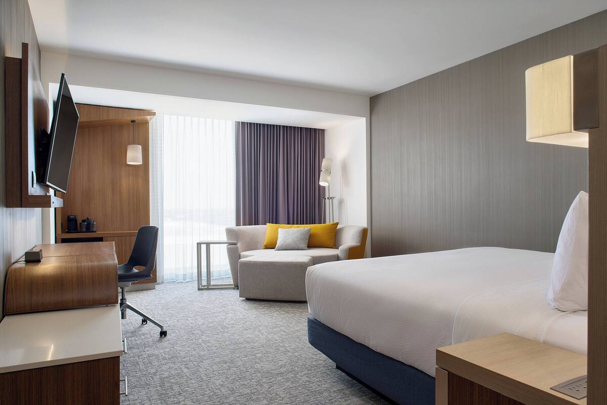 Quarto de hotel com cama, secretária com computador, sofá e uma cadeira.