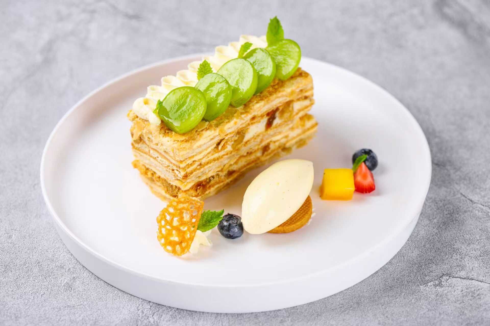 Um prato de sobremesa com um doce em camadas, folhas de menta e pedaços de fruta.