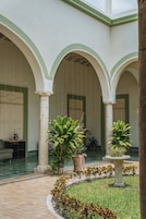 Um pátio com arcos, plantas em vasos, uma fonte e piso de azulejos.