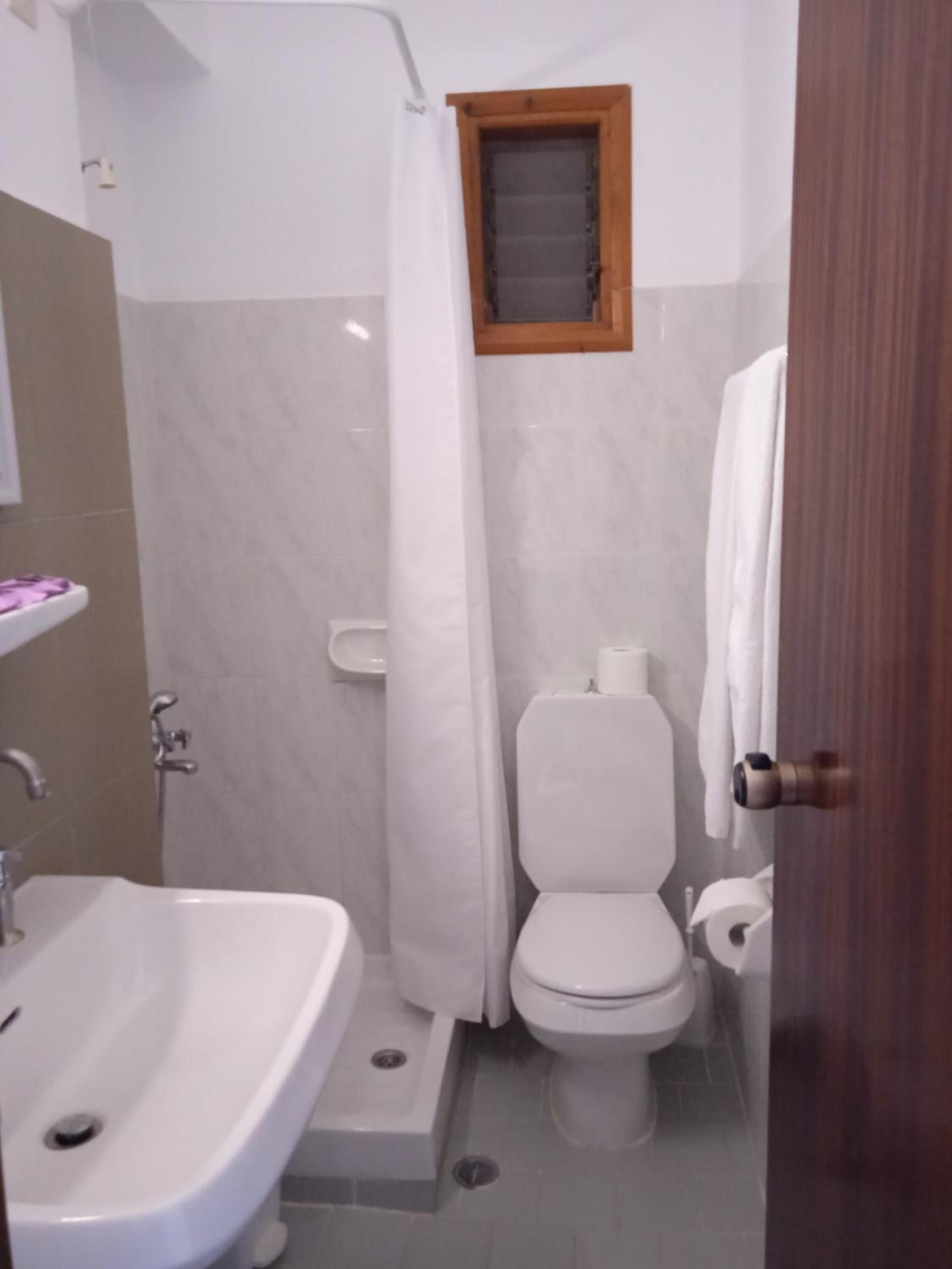 Casa de banho com lavatório branco, sanita e cortina de chuveiro.