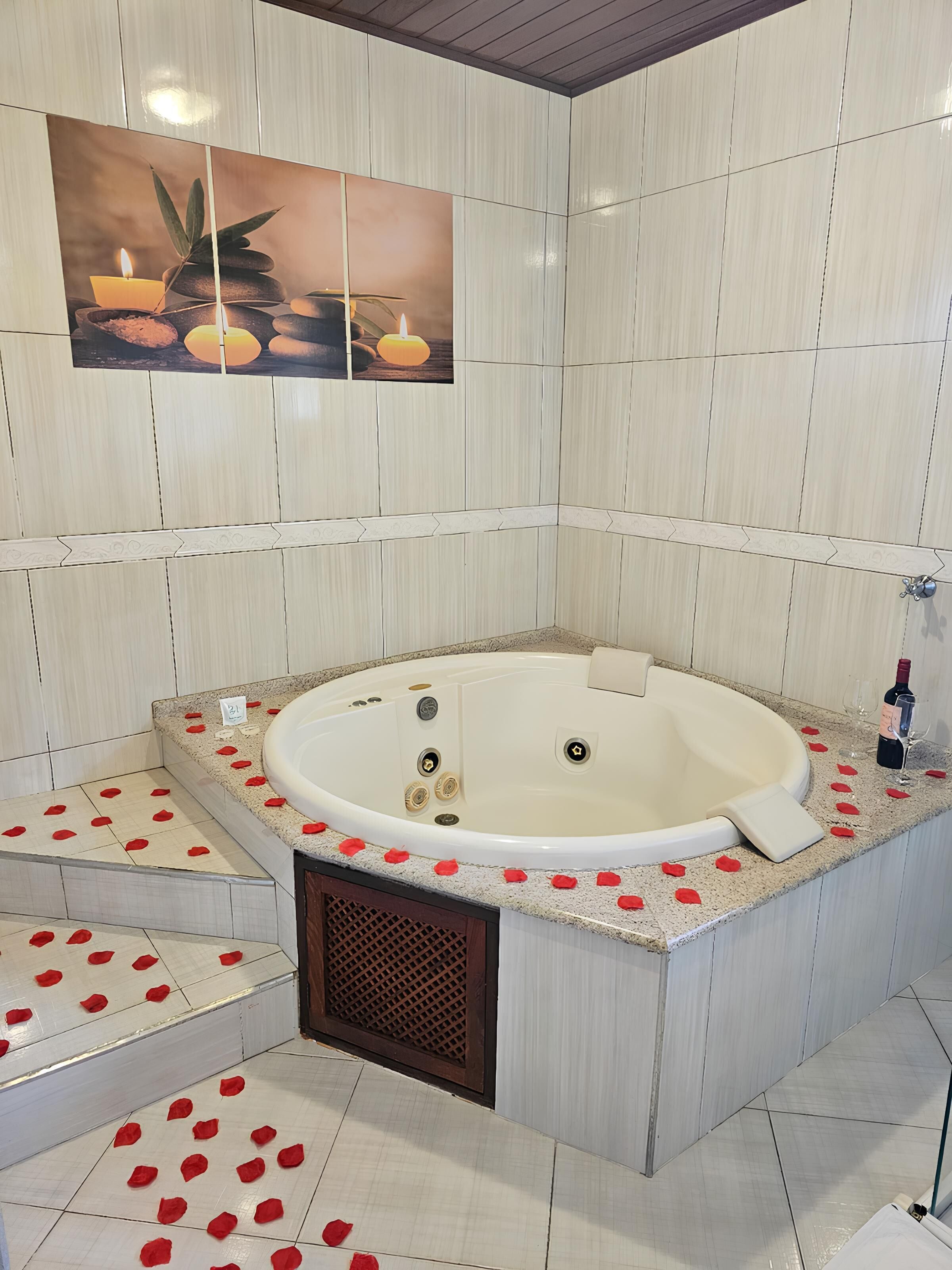 Um quarto de spa com uma banheira grande, pétalas de rosa no chão e uma pintura acima da banheira.
