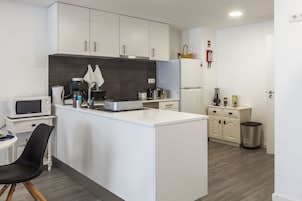Cozinha compacta com armários brancos, uma ilha central, micro-ondas, cafeteira e lixeira.