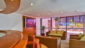 Uma área de estar moderna com mobiliário de vime, um balcão de madeira e uma grande tela de televisão.