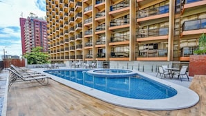 Piscina no terraço com espreguiçadeiras e vista para um arranha-céu.