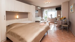 Quarto com cama, escrivaninha e cadeira. Há uma janela com cortinas e vista para o exterior.