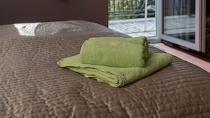 Quarto com cama, toalha verde e vista para o exterior através de uma porta de correr de vidro.